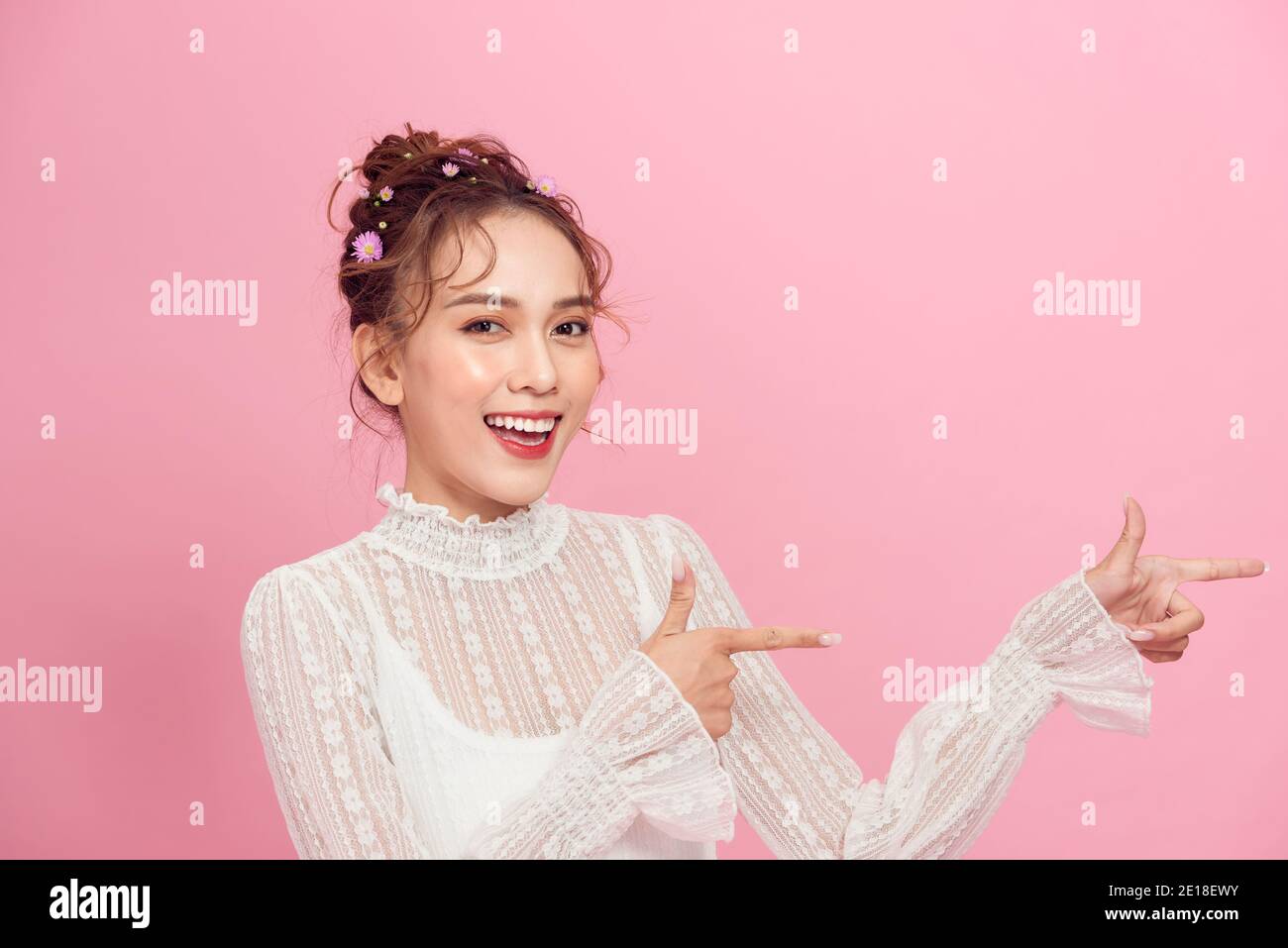 Young pretty chinese woman pointing with forefingers to a copy space ...