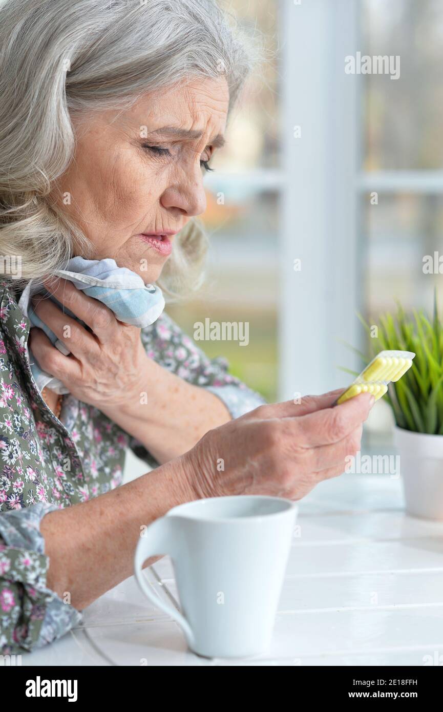 Sick senior woman sitting at table at home with sore throat Stock Photo ...