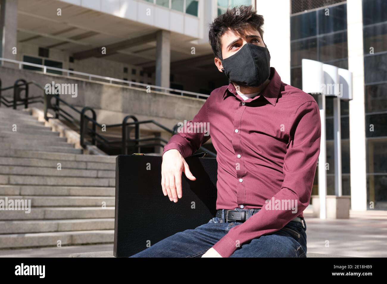 Young business man wearing protective face mask and a suitcase, sitting ...