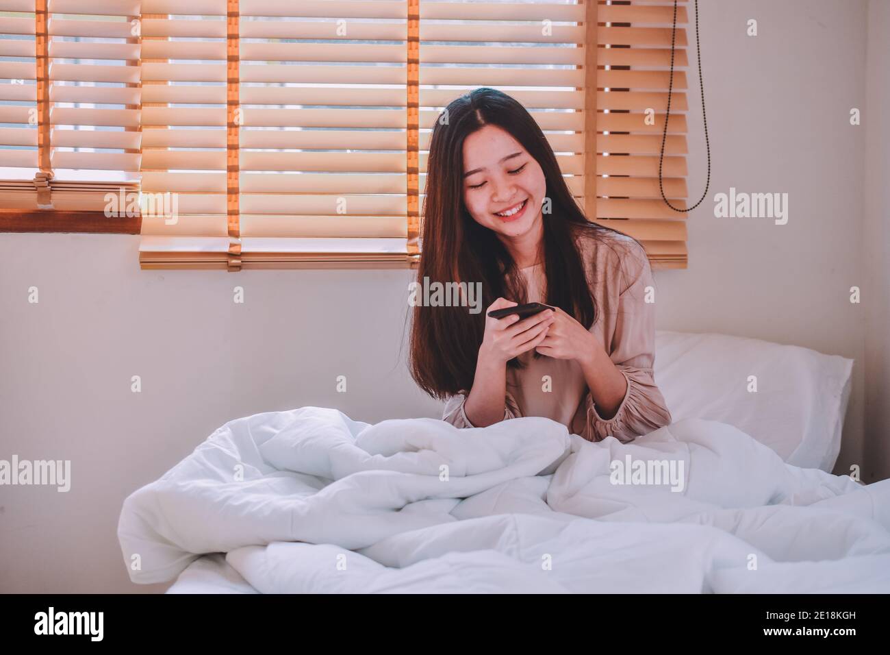 Women holding Mobile smartphone sitting on bed in room Stock Photo - Alamy