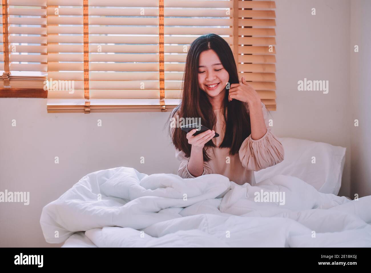 Women holding Mobile smartphone sitting on bed in room Stock Photo - Alamy