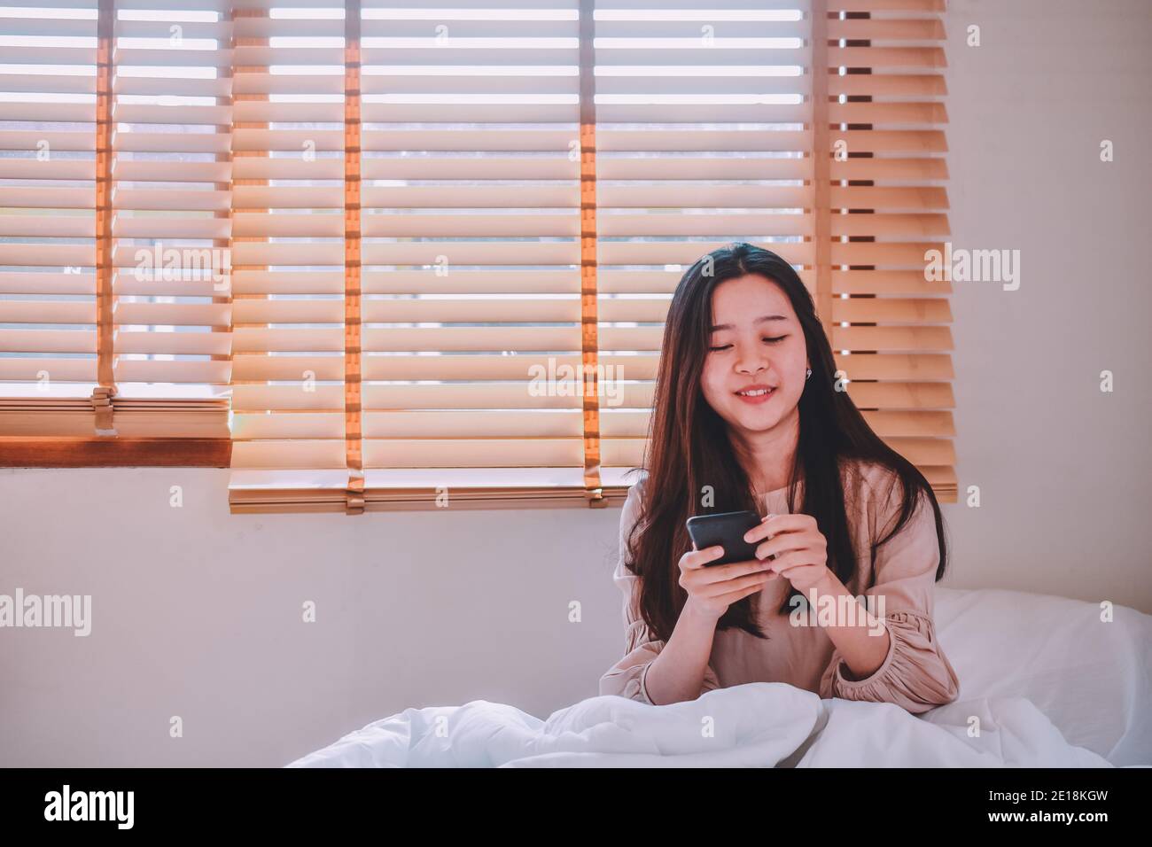 Women holding Mobile smartphone sitting on bed in room Stock Photo - Alamy