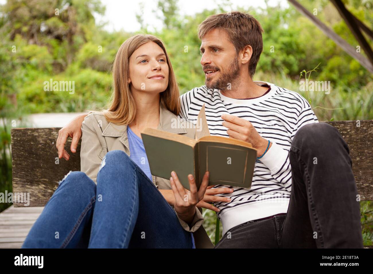 Couple reading book while sitting on bench Stock Photo - Alamy
