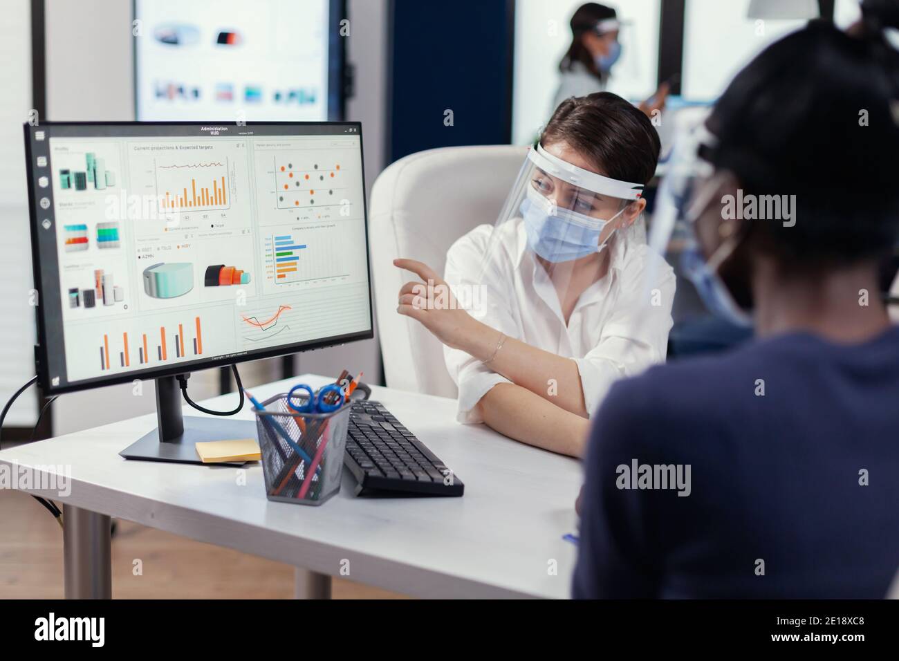Manager sitting at desk pointing at financial graph during discussion ...