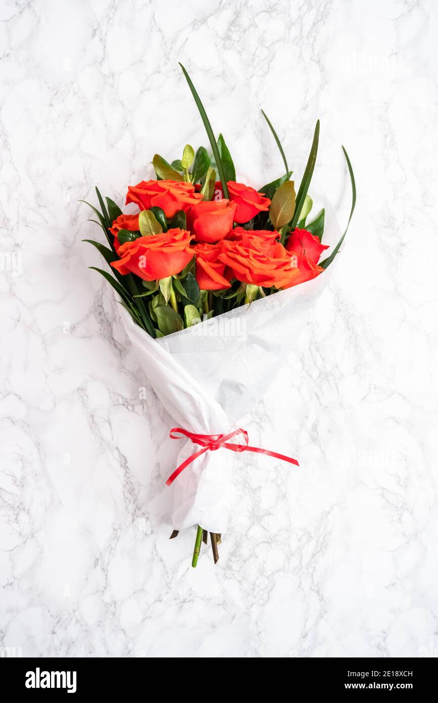Flat lay. Bouquet of red roses and green leaves on a marble background ...
