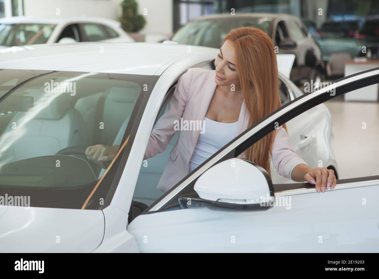 Beautiful long haired woman getting in a new car at dealership. Female ...