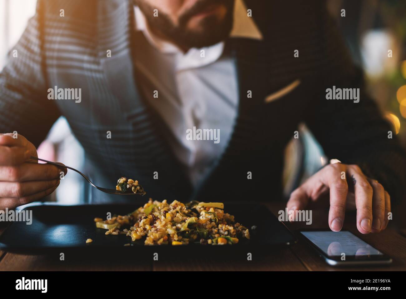 Bearded suited man checking phone while eating food in an elegant ...