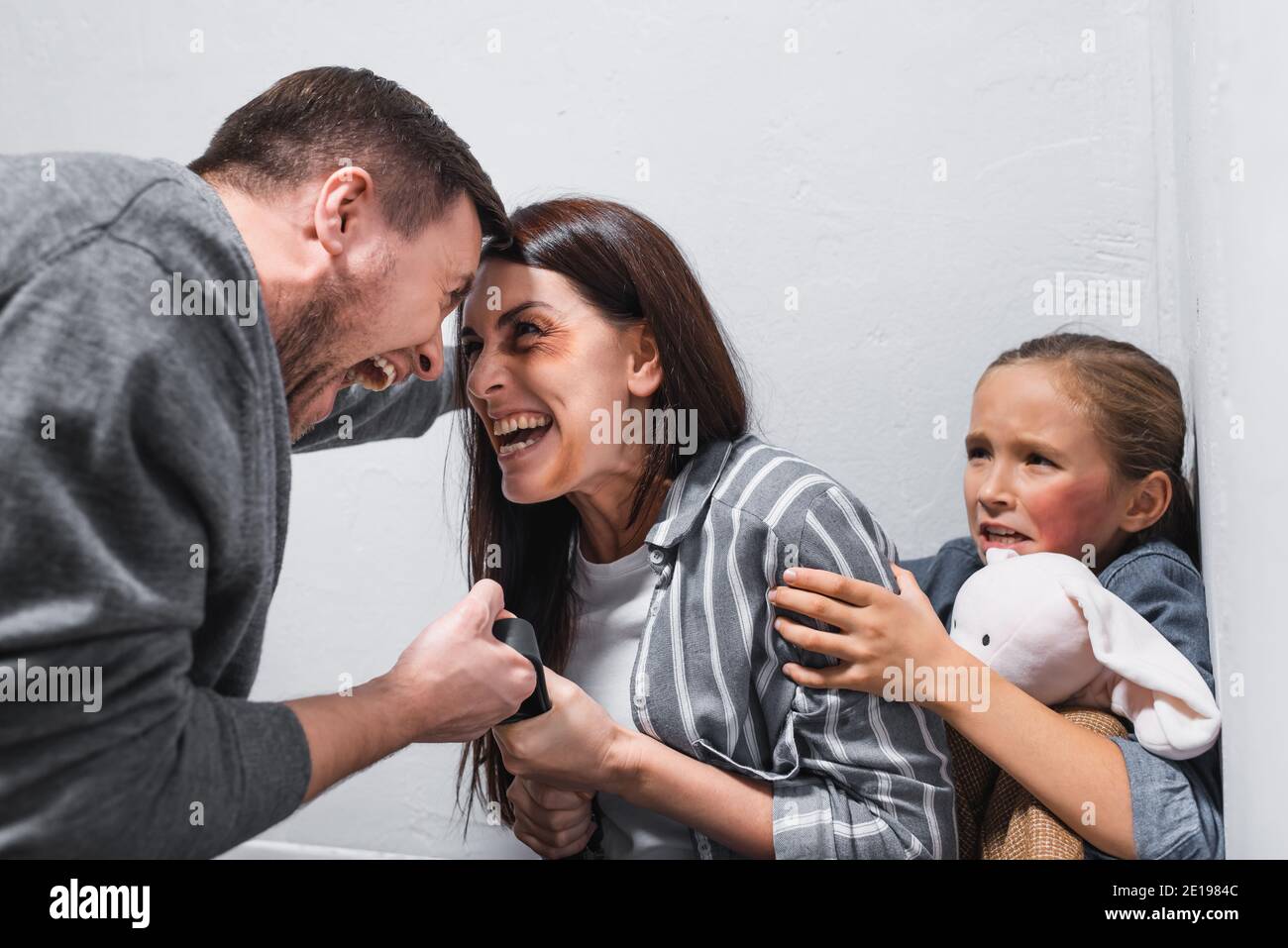 Screaming woman with bruises taking waist belt from husband hands near ...