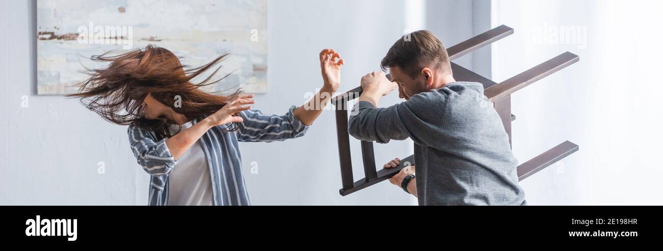 Victim of domestic violence screaming near husband with chair at home ...