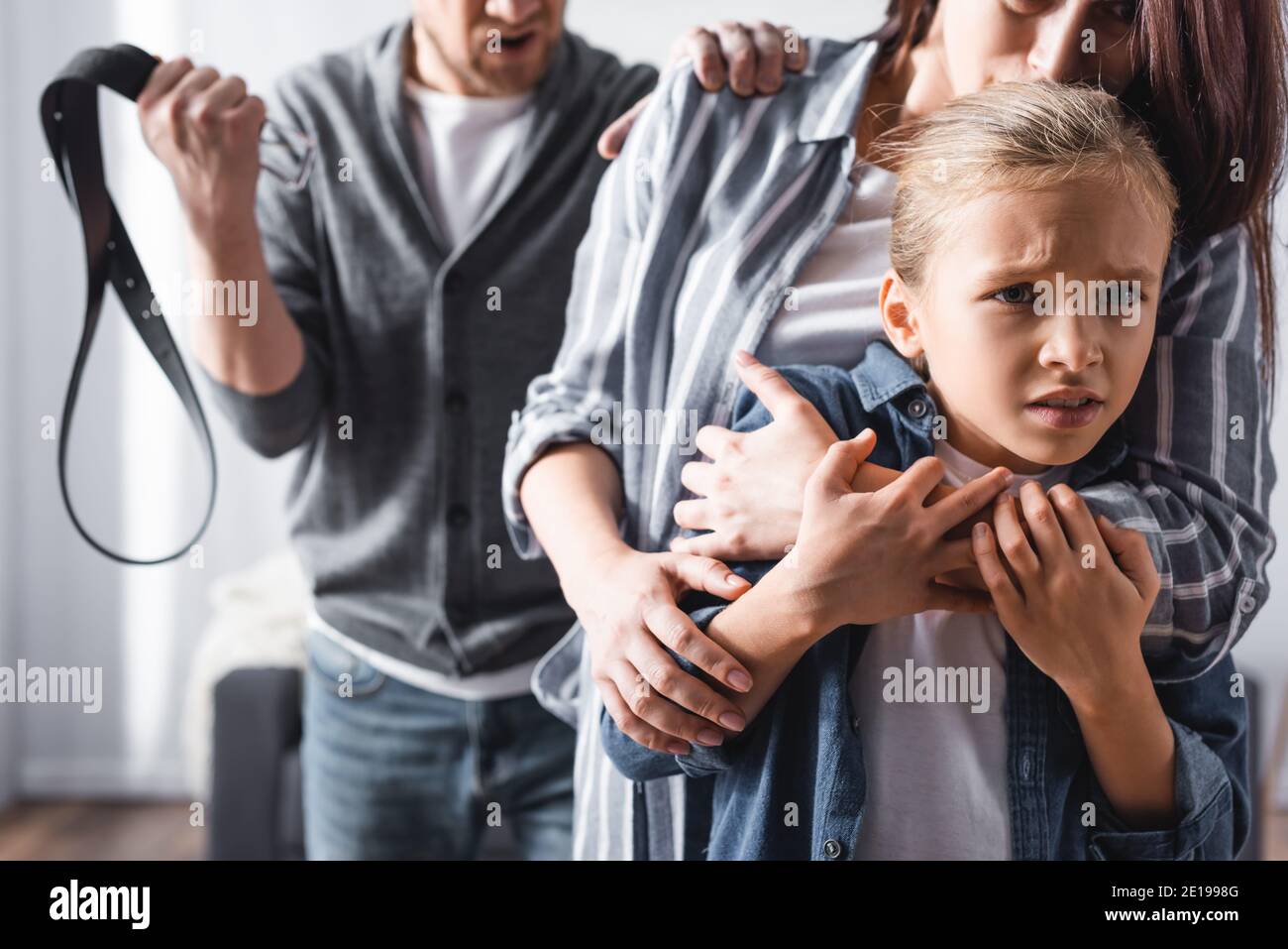 Scared child embracing mother near angry father holding waist belt on ... Scared child embracing mother near angry father holding waist belt on ...