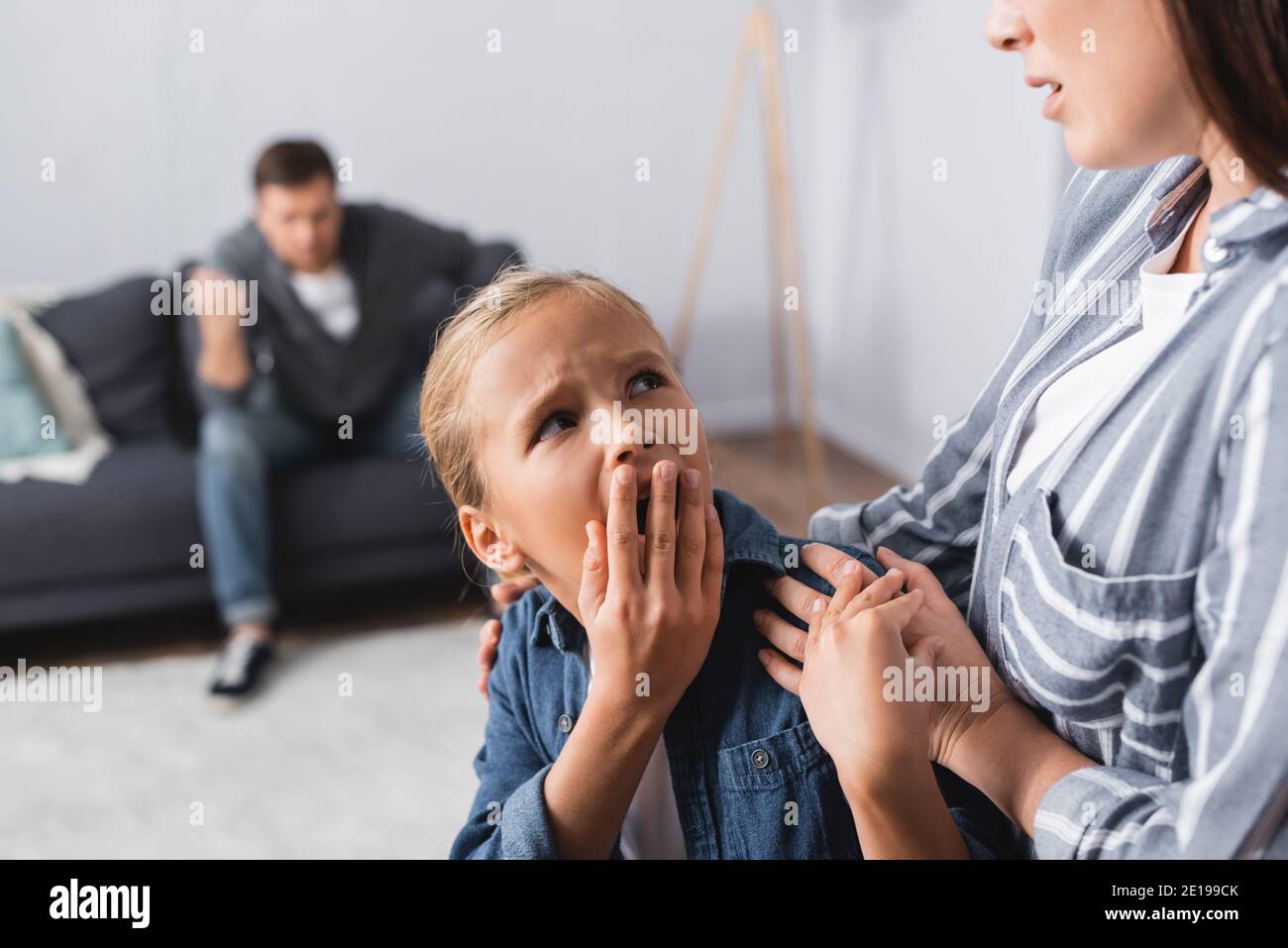 Woman hugging scared kid near abusive husband on blurred background at ...