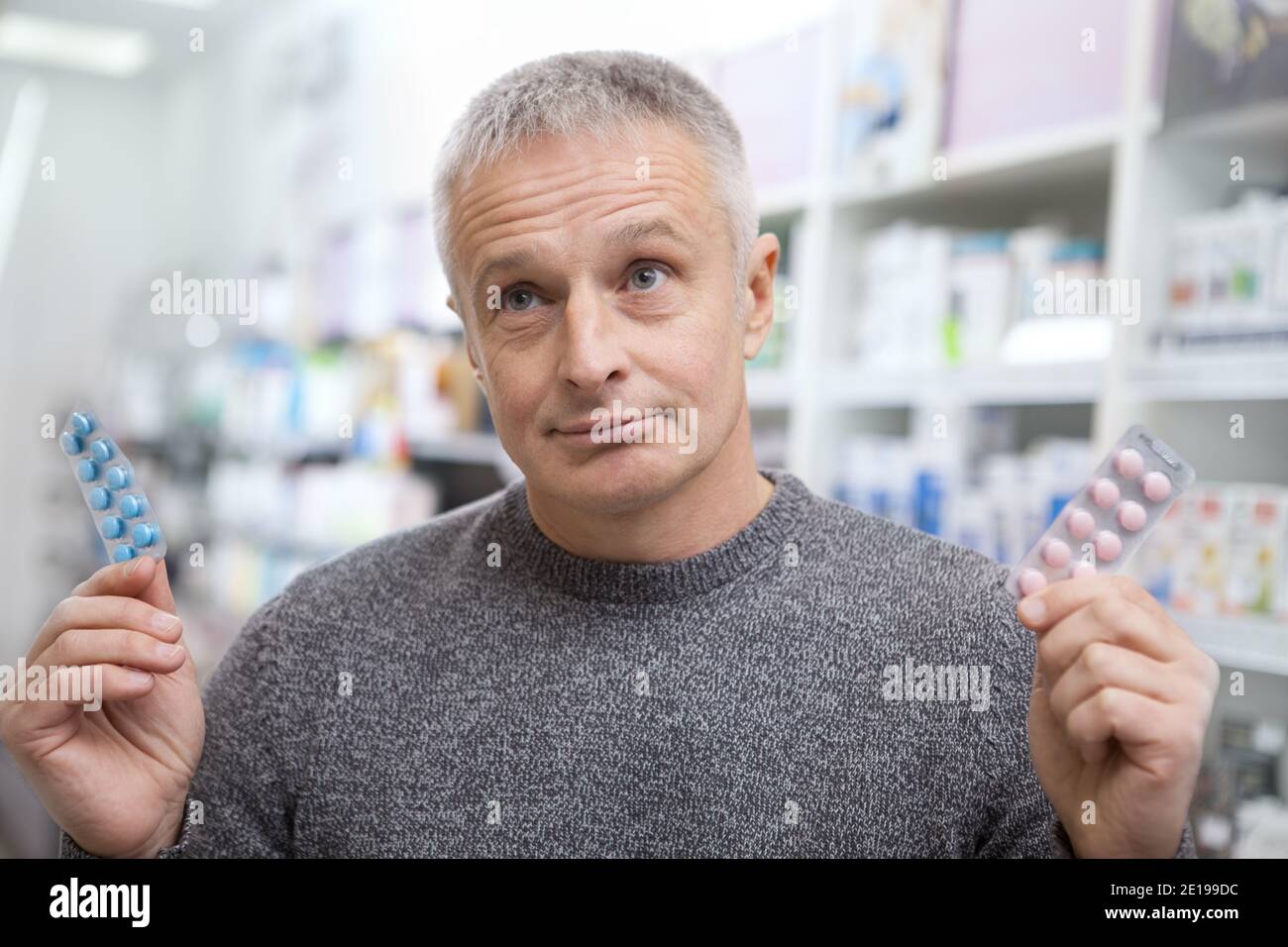 Mature man looking confused, choosing between two different blisters of ...