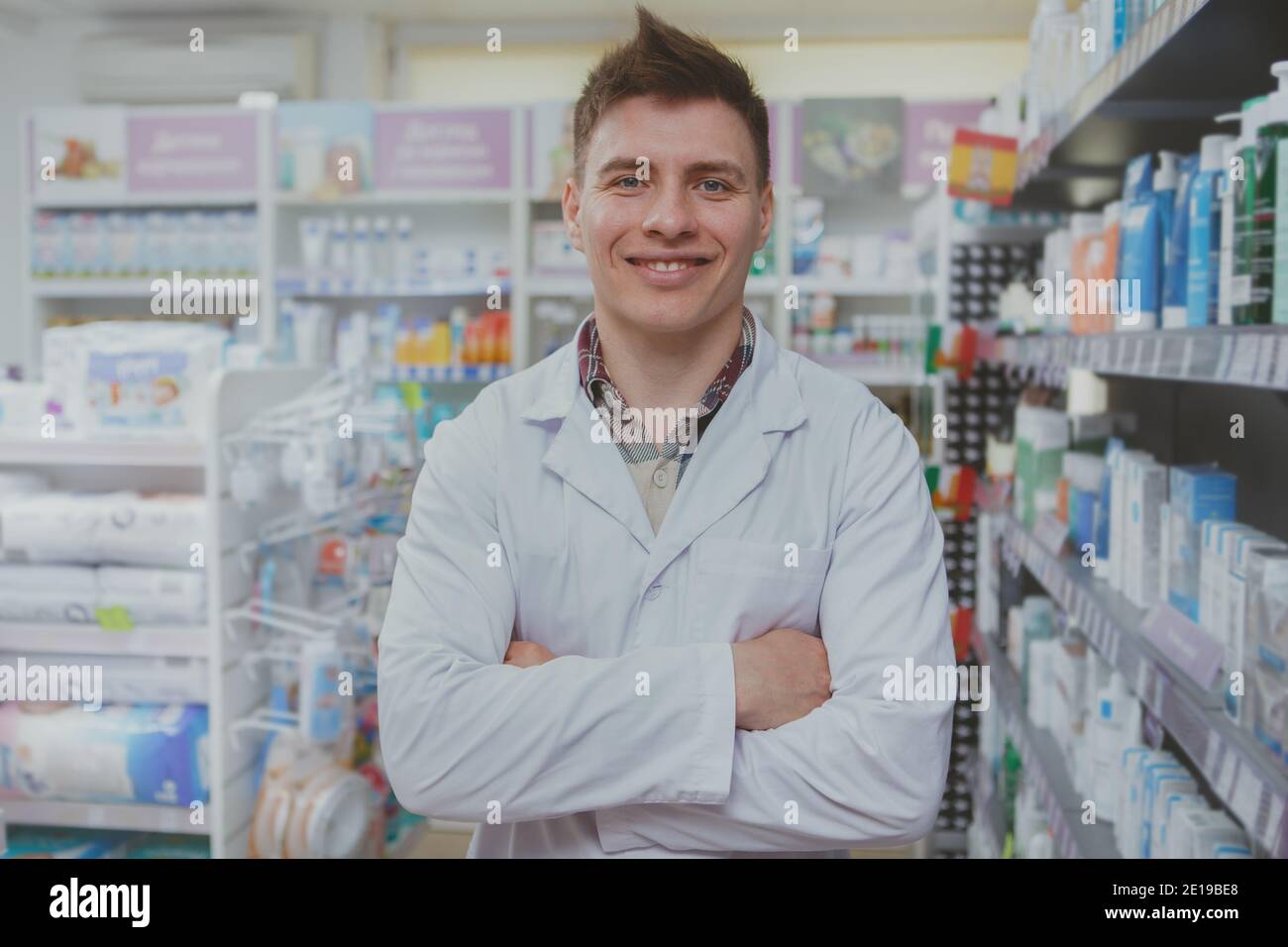 Happy handsome pharmacist standing with arms crossed at the drugstore ...