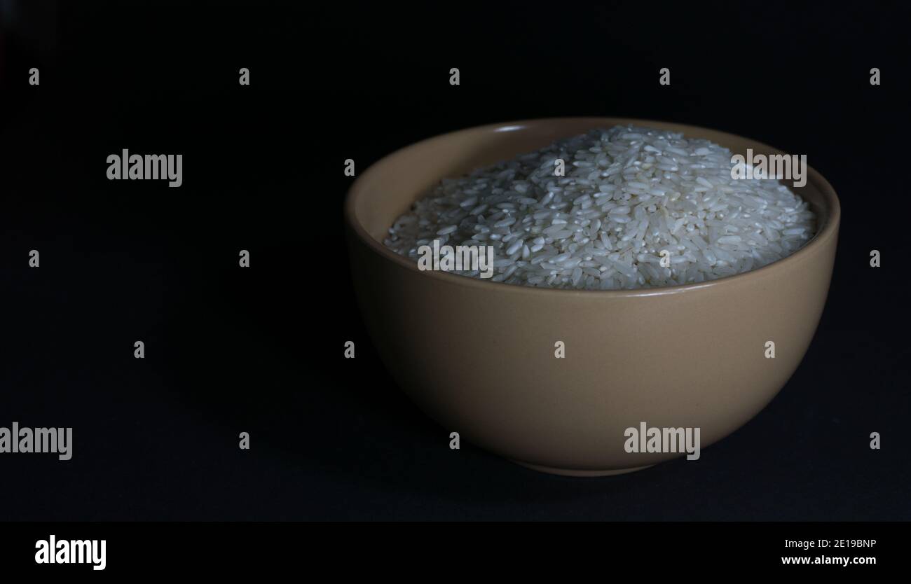 White uncooked rice in a beige bowl with scattered grains nearby on a ...