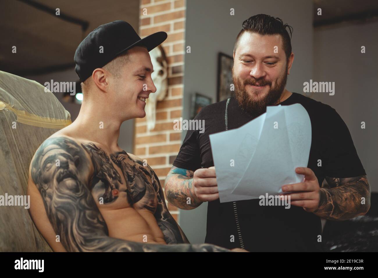 Cheerful bearded tattoo artist smiling joyfully talking to his client ...