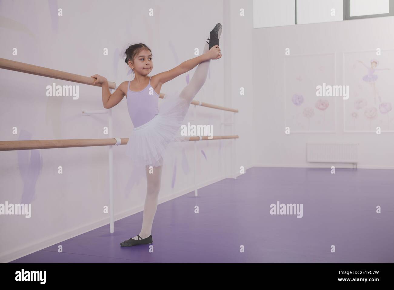 Full length shot of a cute young ballerina stretching at ballet school ...