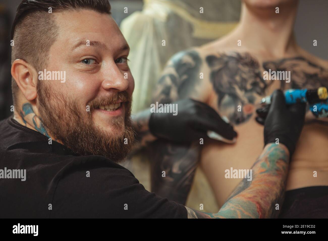 Close up of a cheerful bearded tattoo artist smiling to the camera over ...