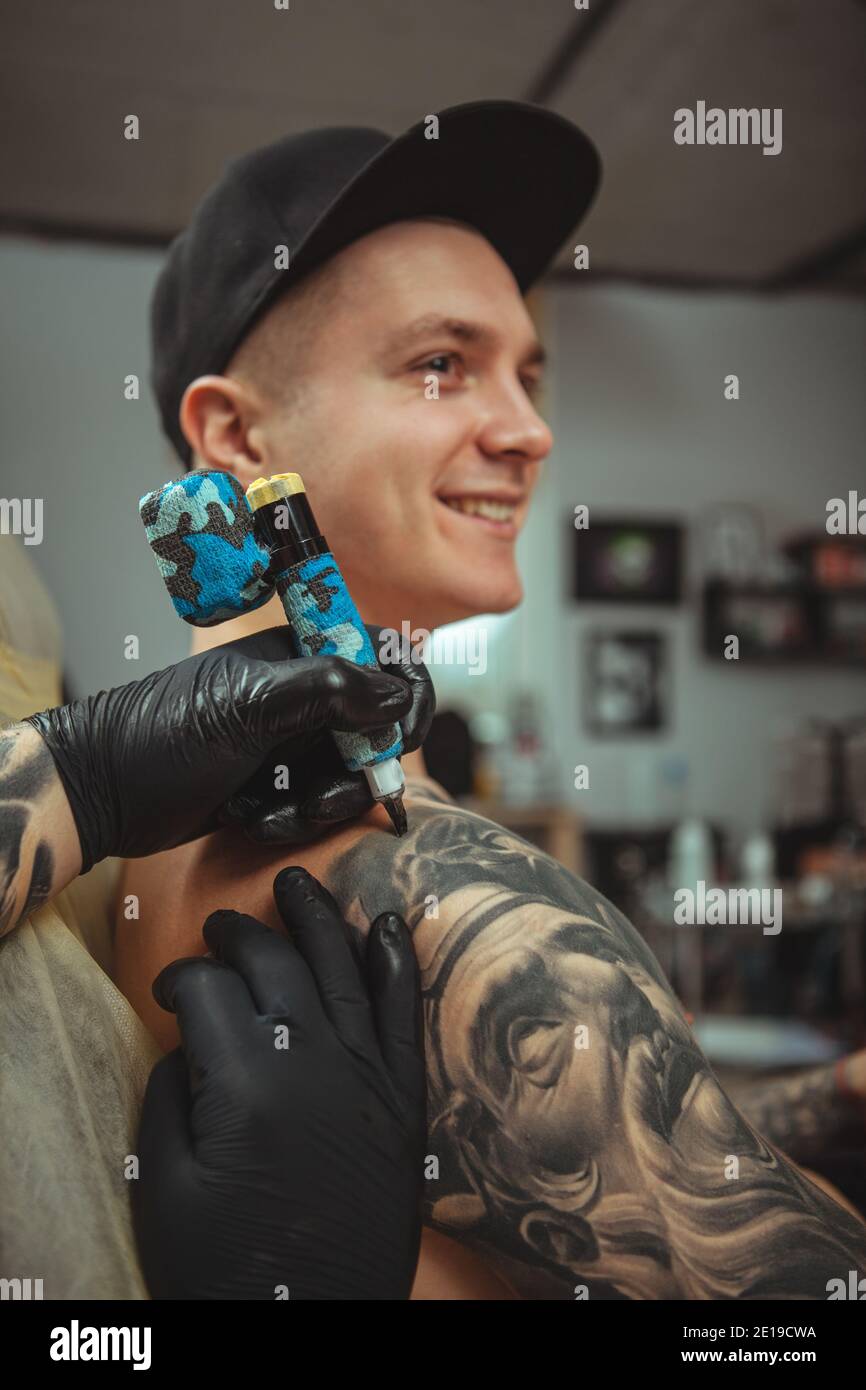 Vertical close up of a handsome young man smiling, getting tattooed on ...