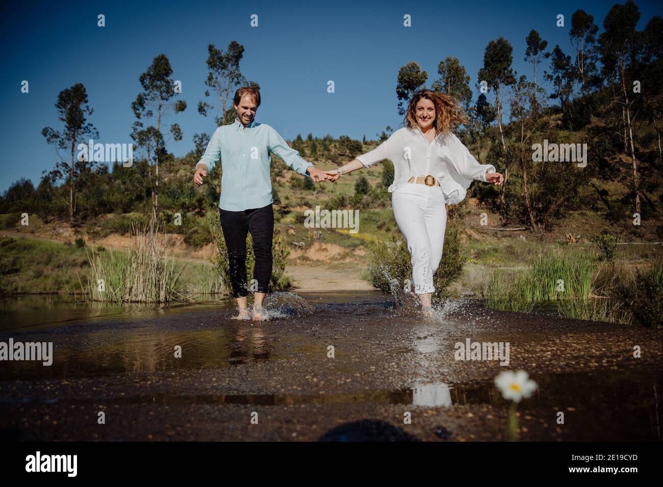 Couple running through the water, splashing each other. Welcoming the ...