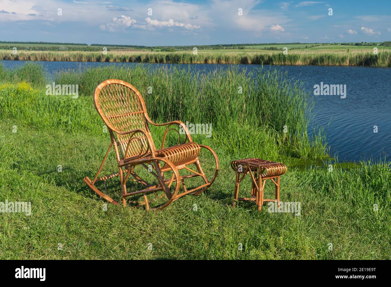 Empty wicker rocking-chair standing next to small wicker hadnmade stool ...