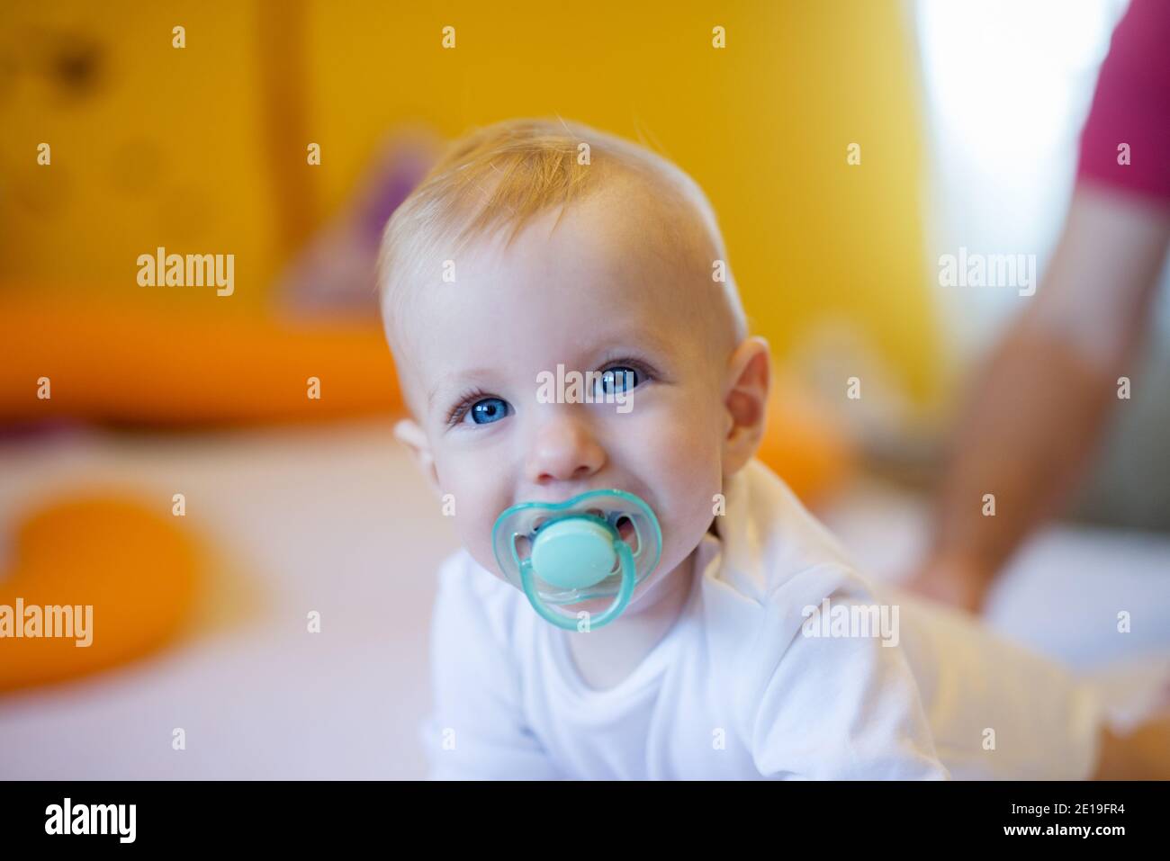 Beautiful pretty blue eyed baby kid with pacifier sitting on the bad ...