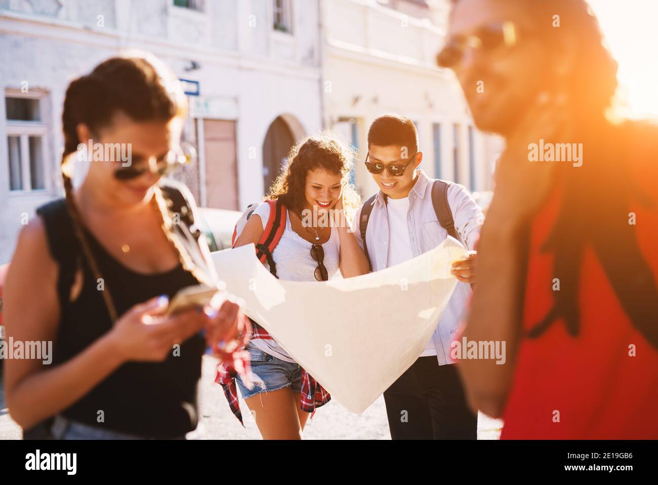 Four youthful friends searching for a direction on a map while enjoying ...