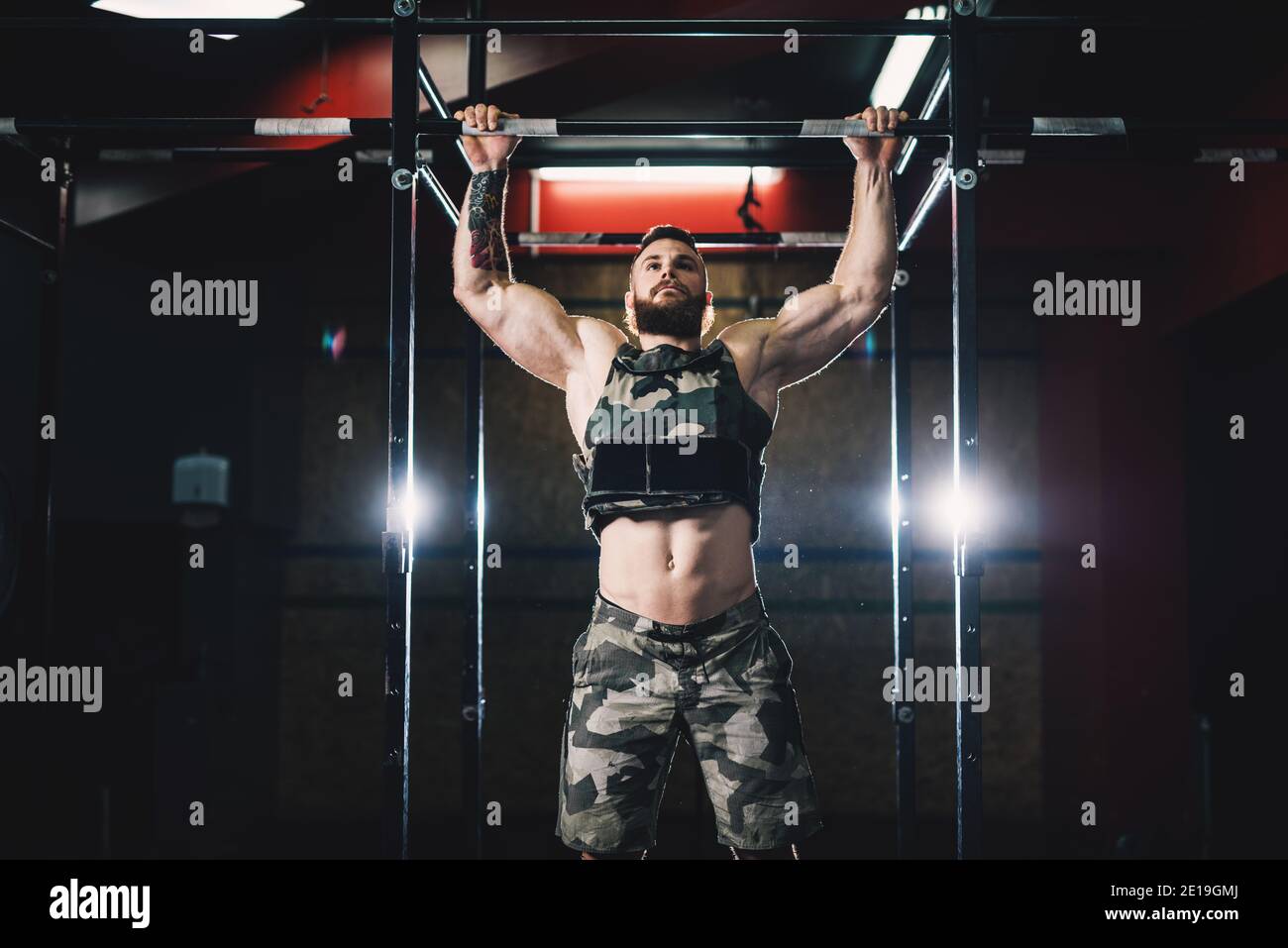 Active powerful muscular bodybuilder guy in military vest doing pull ...