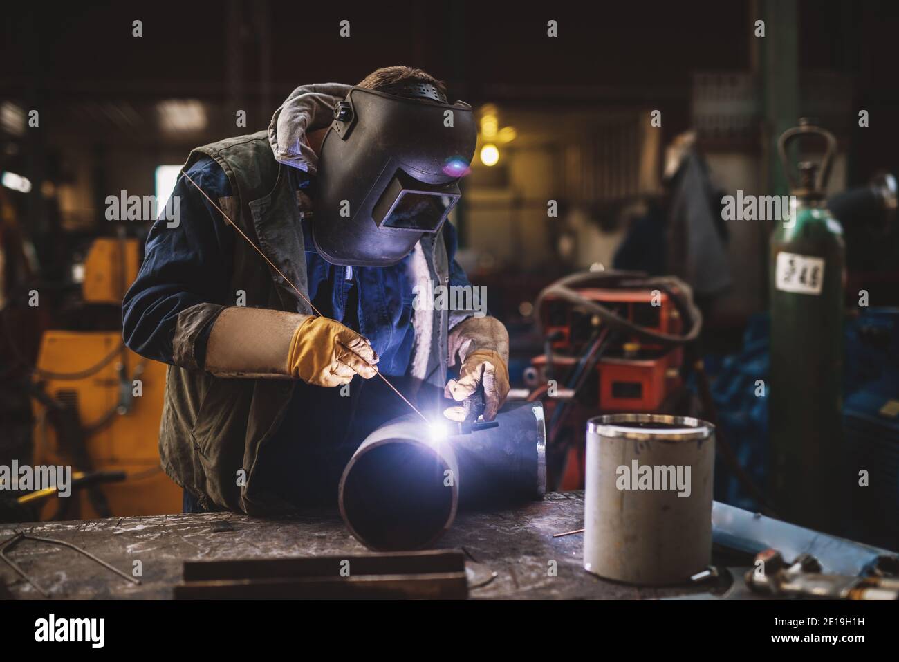 Welder in protective uniform and mask welding metal pipe on the ...