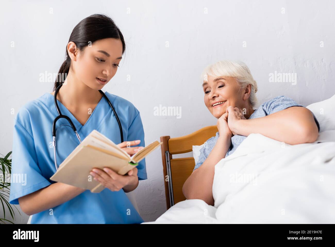 asian nurse reading book to cheerful elderly woman in hospital Stock ...