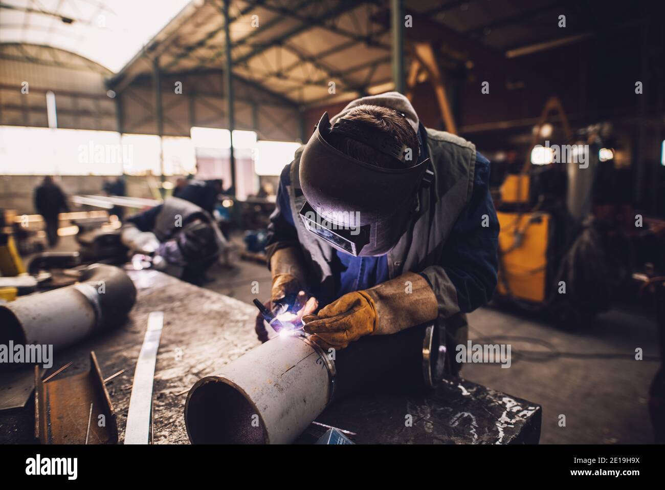 Welder in protective uniform and mask welding metal pipe on the ...