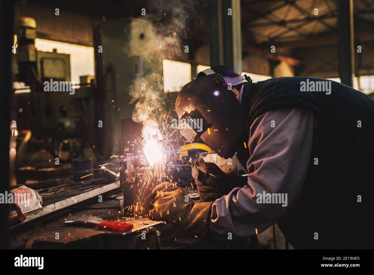 Welder in protective uniform and mask welding metal pipe on the ...