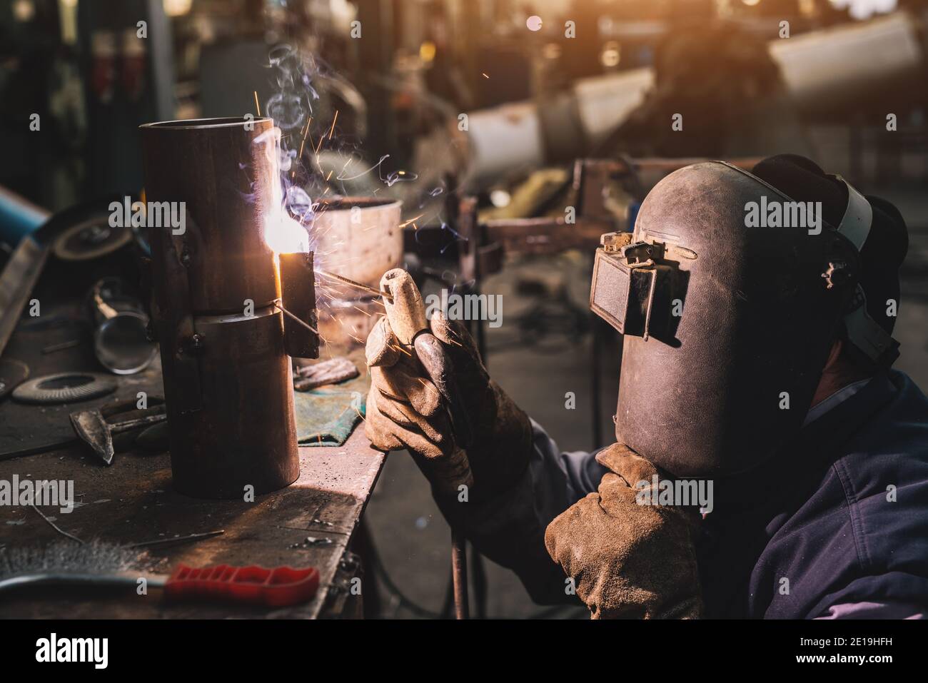 Welder in protective uniform and mask welding metal pipe on the ...