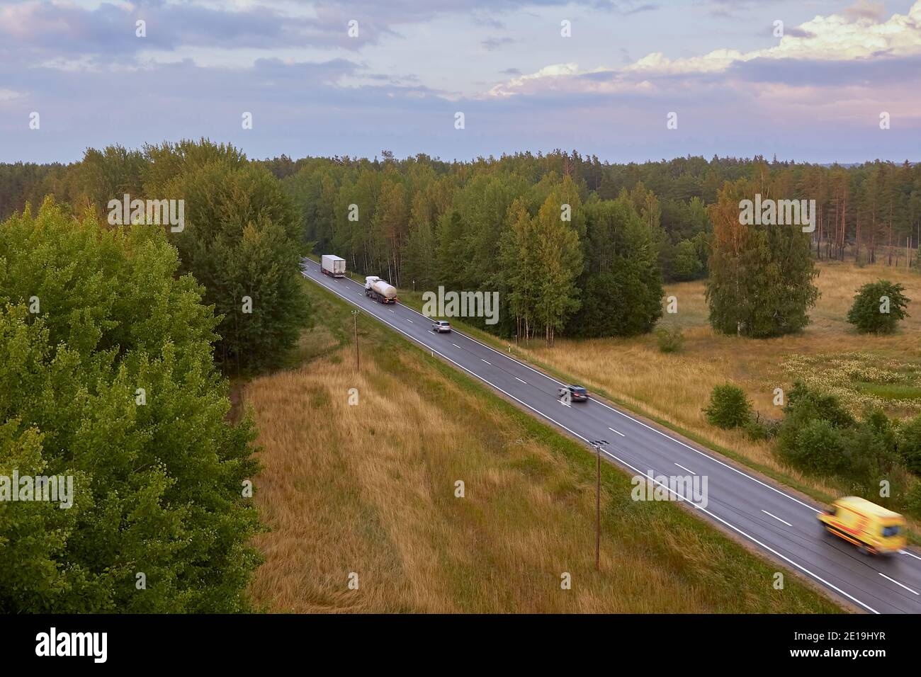 Driving cars on a rural asphalt road next to forest in evening Stock ...