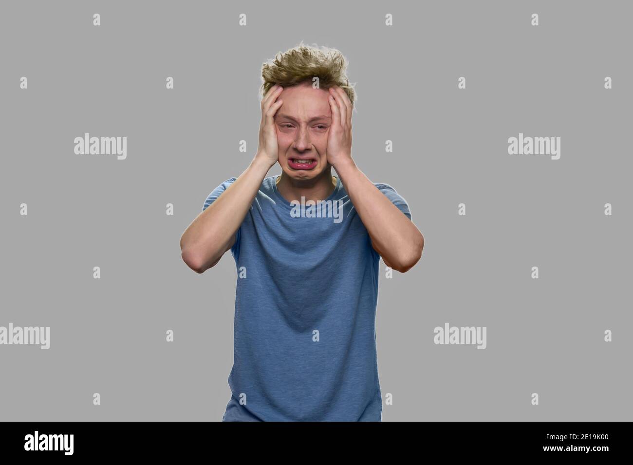 Depressed teen boy crying on gray background Stock Photo - Alamy