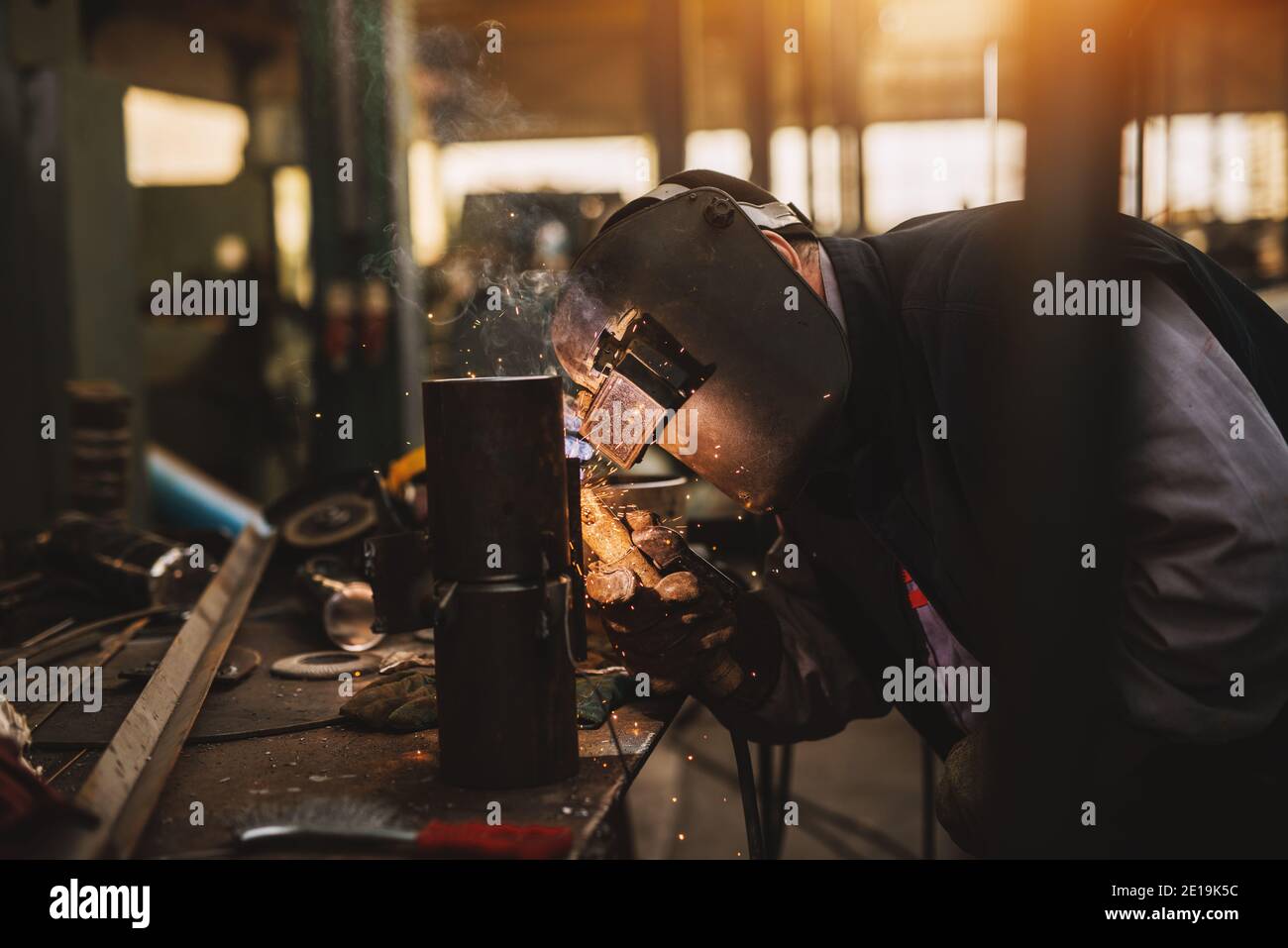 Welder in protective uniform and mask welding metal pipe on the ...