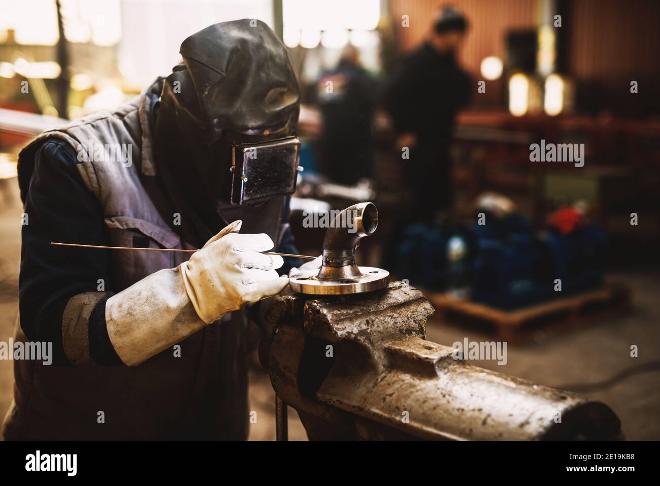 Welder in protective uniform and mask welding metal pipe on the ...
