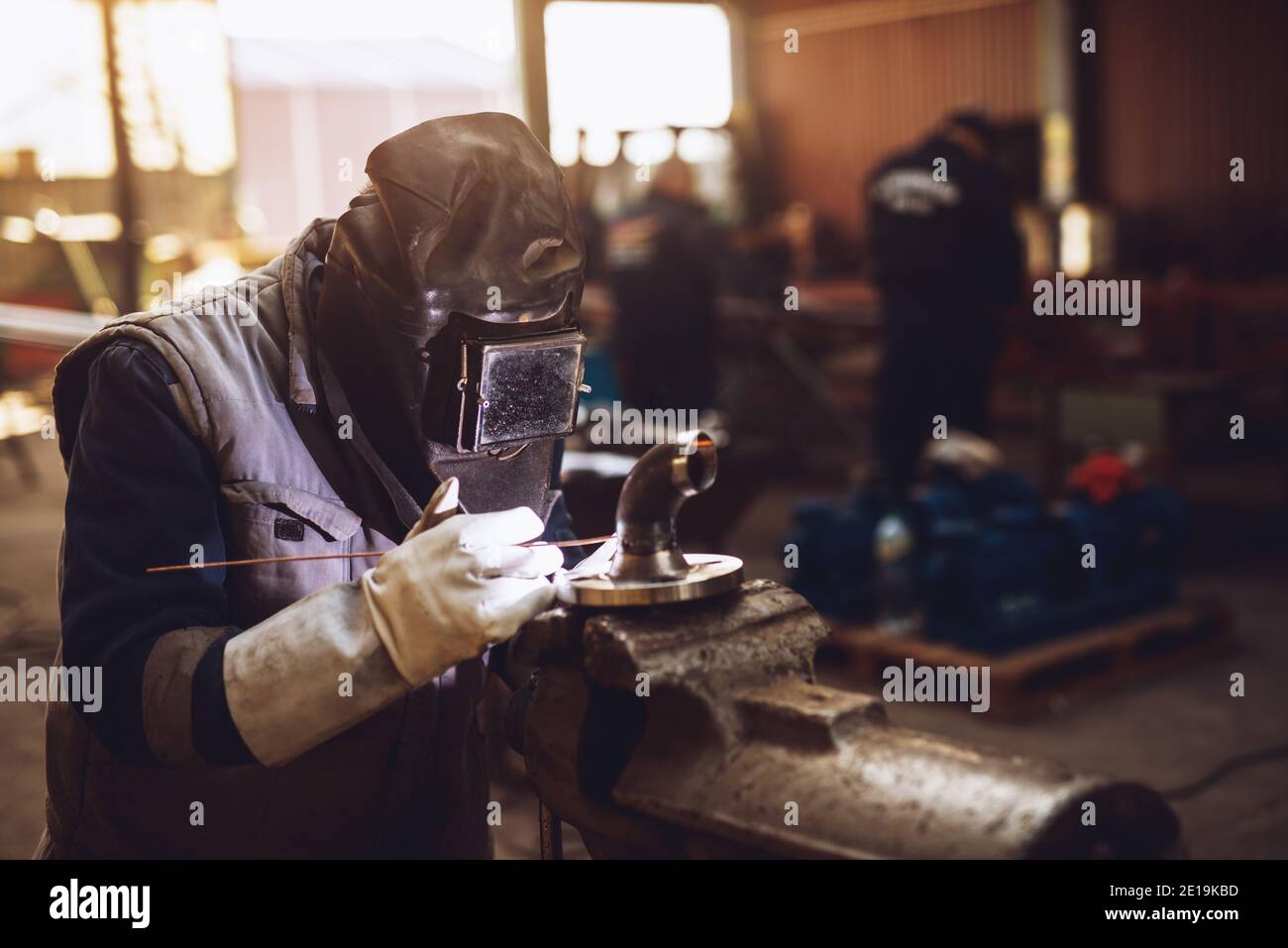 Welder in protective uniform and mask welding metal pipe on the ...