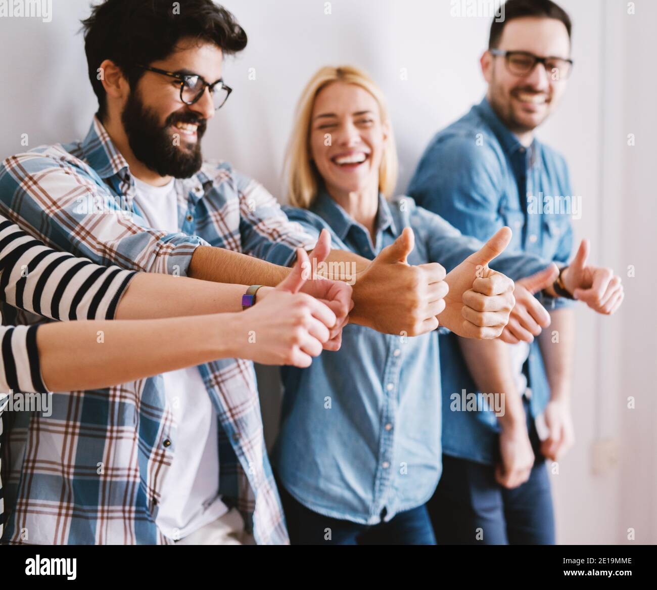 Group of joyful excited young people holding thumbs up while waiting or ...