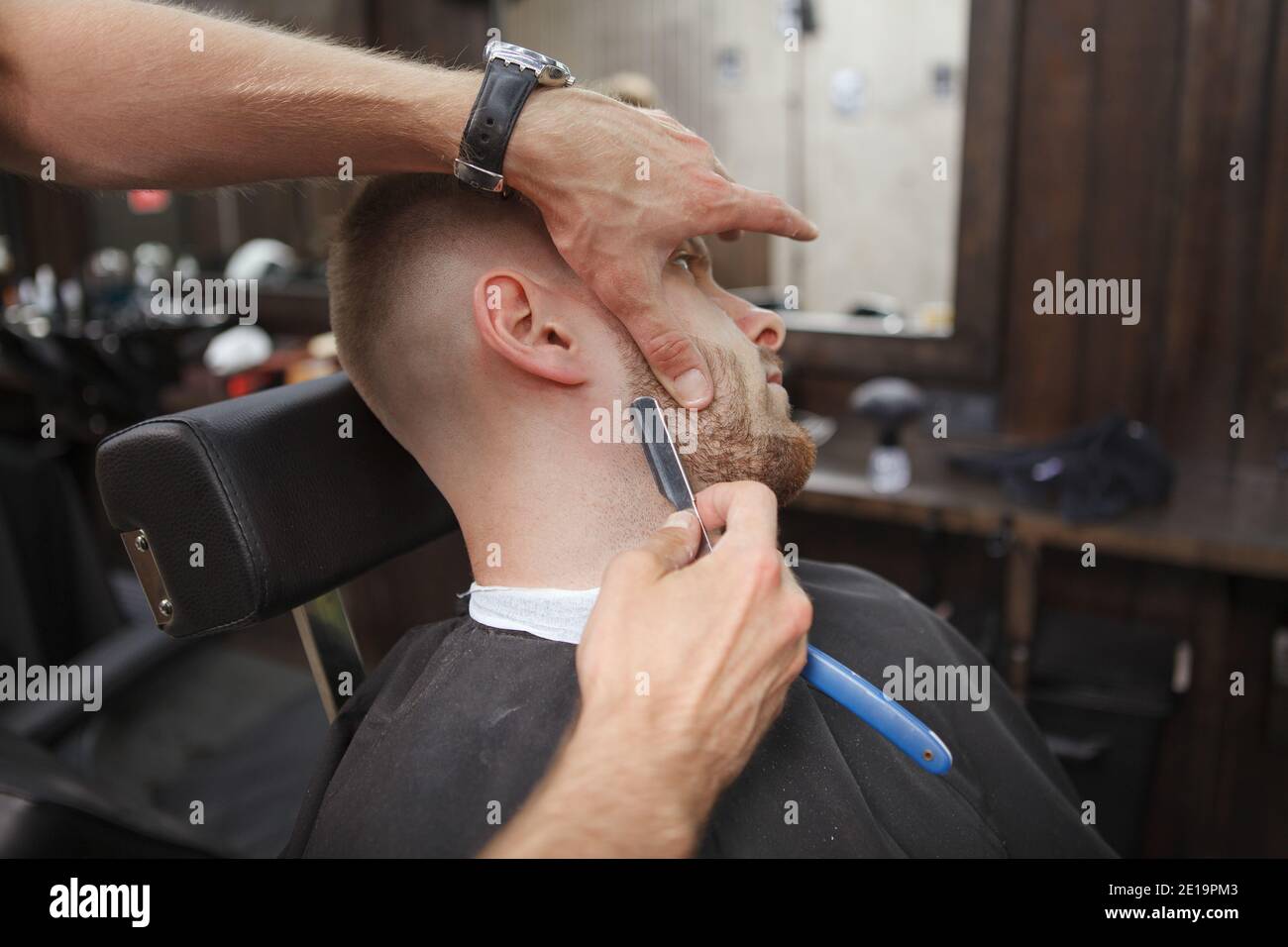 Unrecognizable barber using razor blade, shaving beard of male client ...