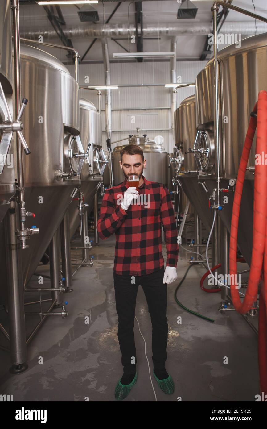 Vertical full length shot of a professional brewer standing near beer ...
