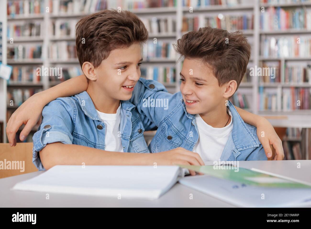 Happy young twin brothers laughing, hugging at the library while doing ...