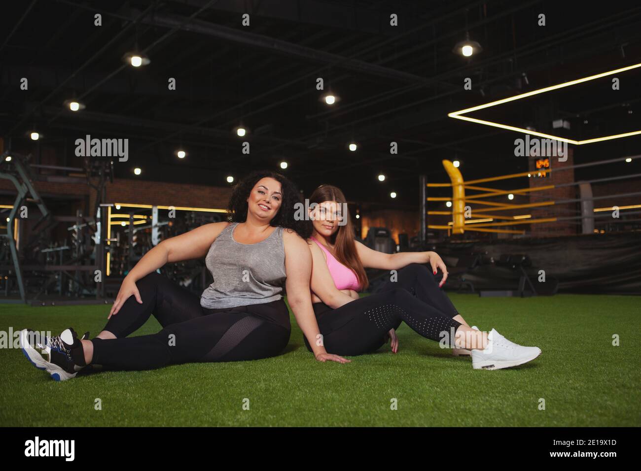 Two beautiful healthy happy plus size fitness women resting at the gym ...