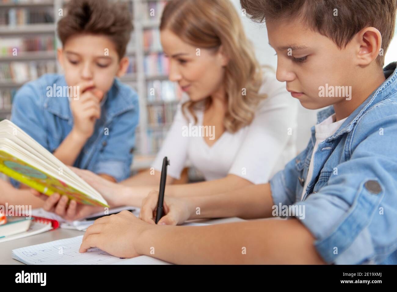 Close up of a young boy writing in his textbook, his mom and twin ...