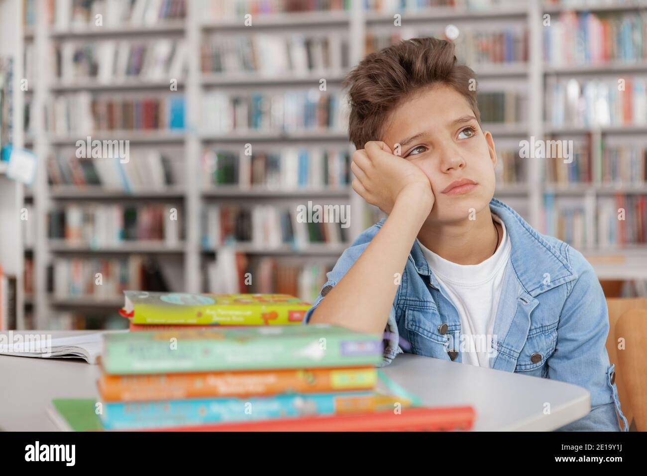 Sad young boy looking away, sitting alone at the library in front of ...
