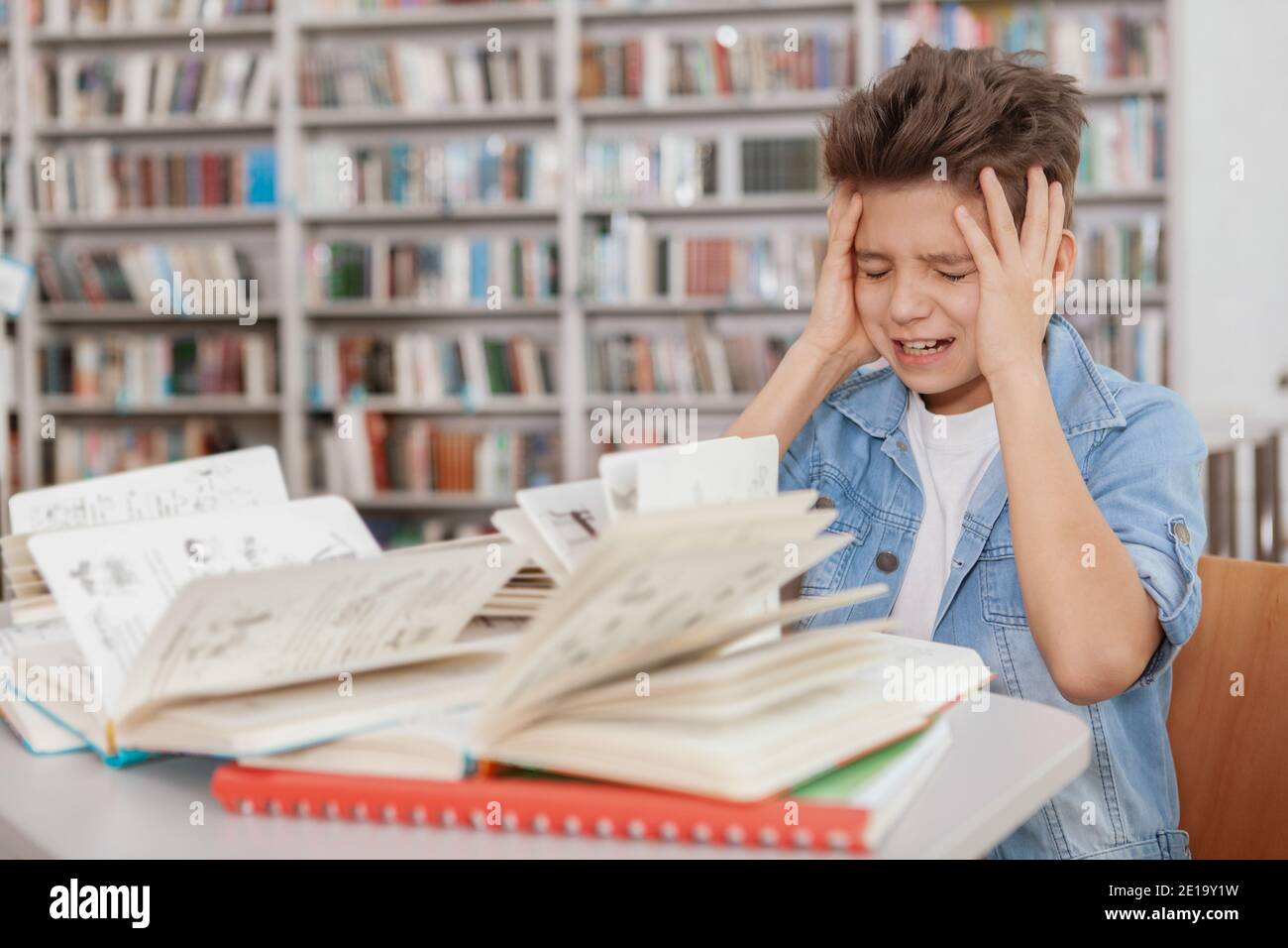 Young boy stressing out over pile of books and textbooks on his desk ...