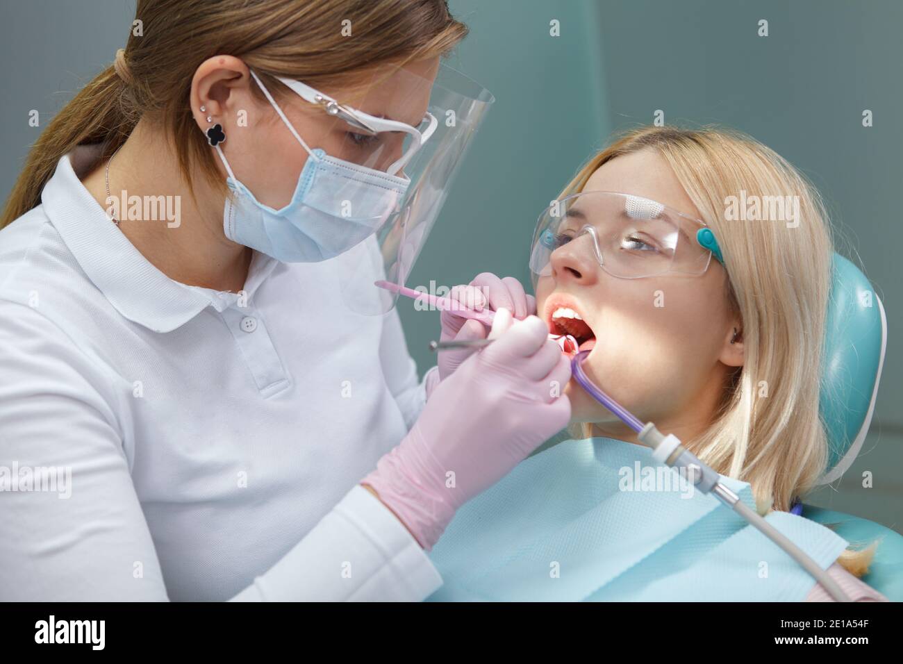 Young woman wearing protective glasses while dentist examining her ...