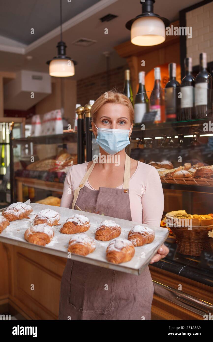Vertical portrait of a female baker wearing medical face mask, carrying ...