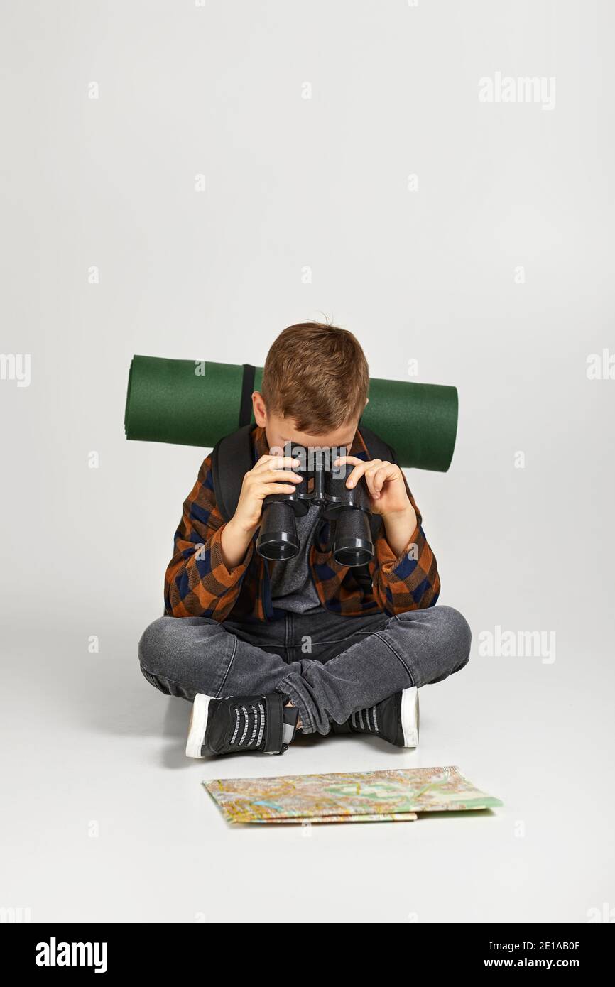 Little boy tourist with backpack looking through a binoculars at map ...