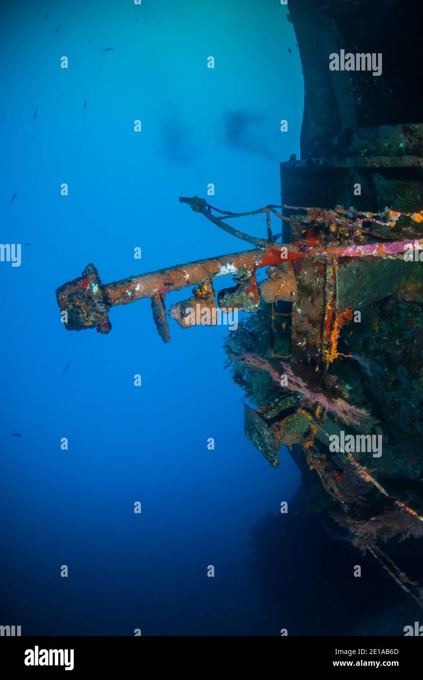 A large, upturned shipwreck on the sea floor near a tropical coral reef ...