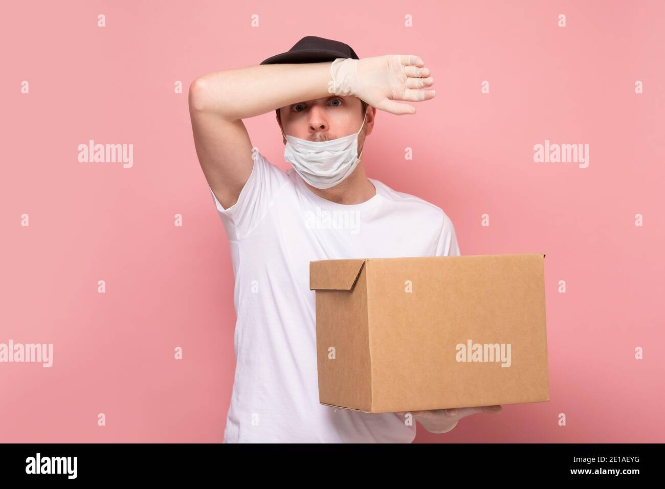 Tired caucasian man is holding a heavy box, wiping the sweat. Studio ...